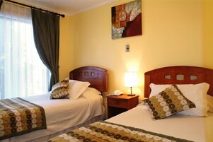 Quarto de hotel com duas camas, cada uma com colcha estampada, cabeceira de madeira, luminária de cabeceira e um quadro na parede.