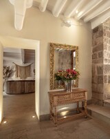 Um corredor com parede de pedra, um console de madeira com espelho e um vaso de flores.