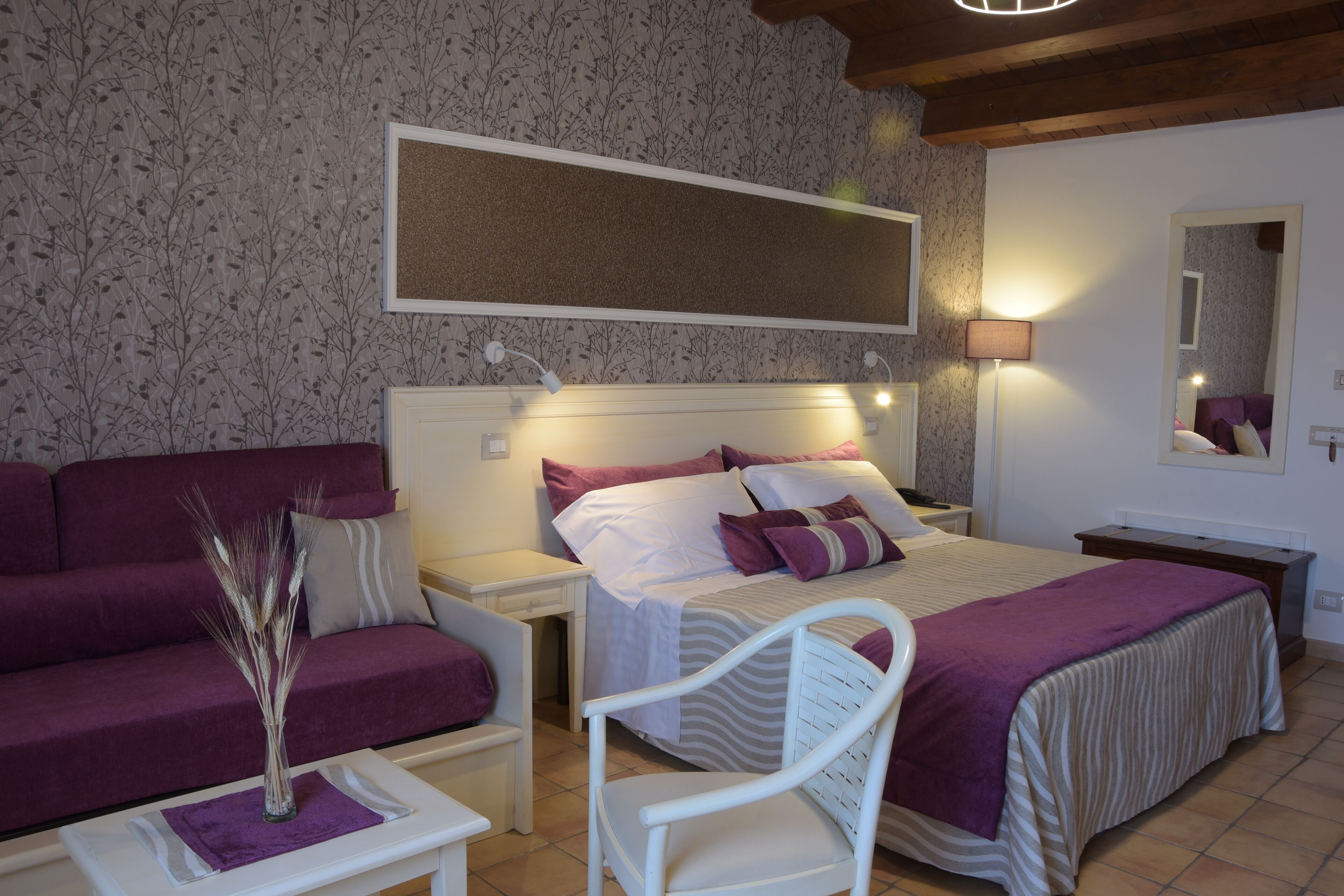Um quarto com uma cama, mesa de cabeceira, cadeira, espelho e prateleira na parede.