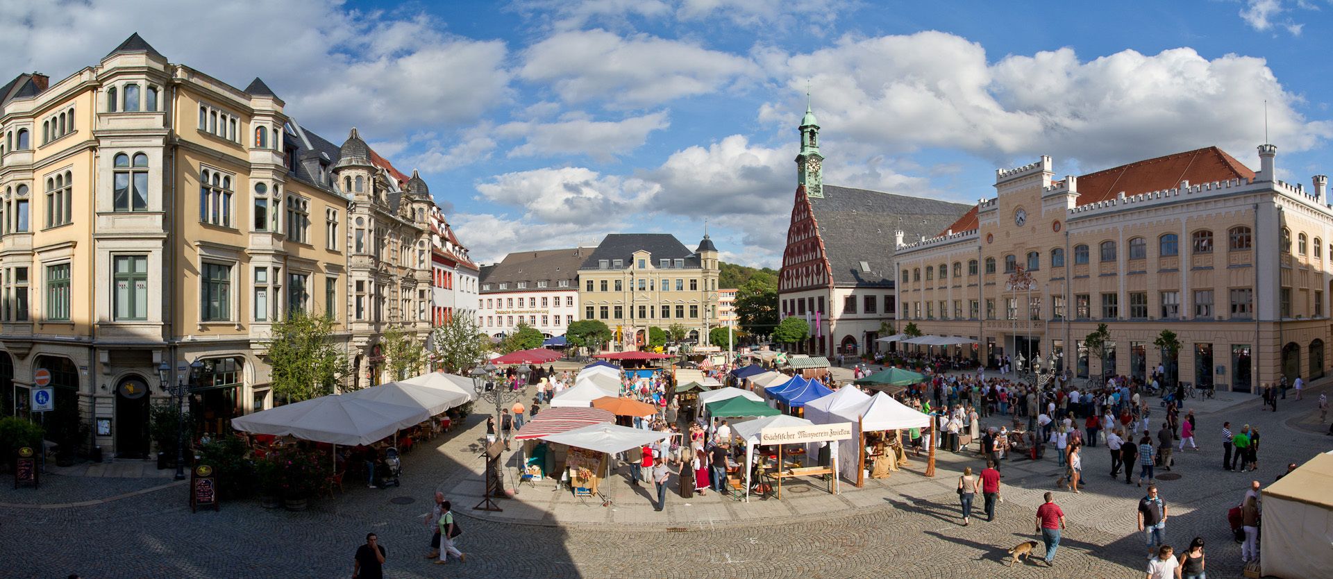 Uma praça movimentada com edifícios históricos, calçamento de pedras e bancas de mercado ao ar livre.