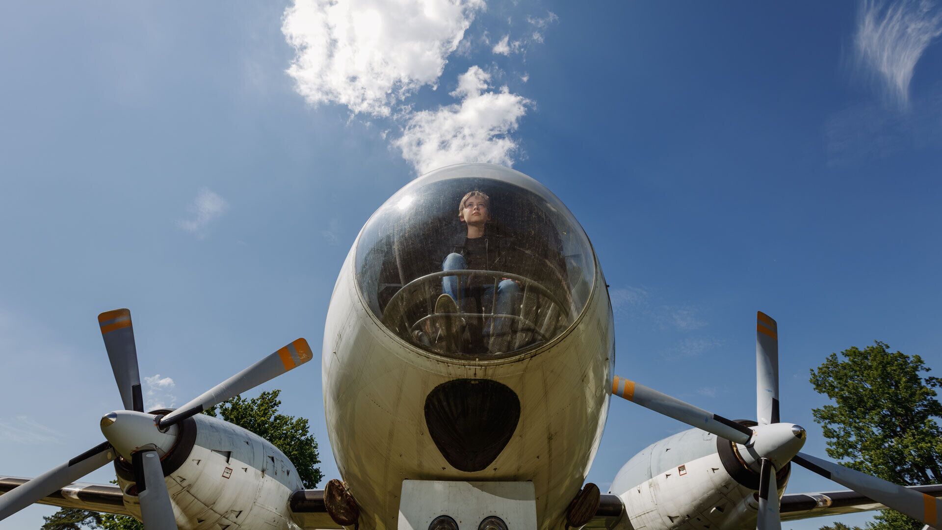 Um avião com cobertura transparente para a cabine, hélices e um piloto visível.
