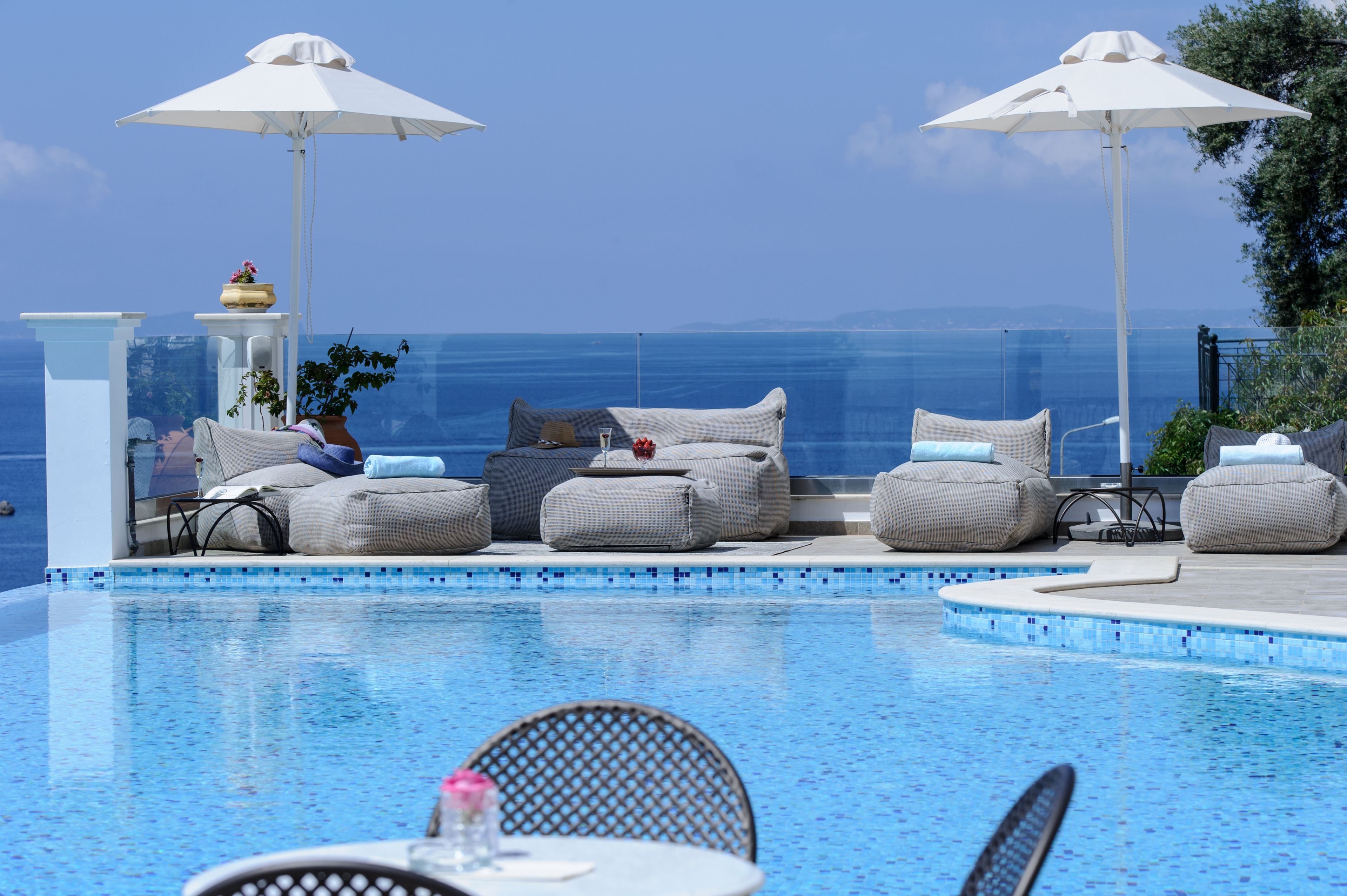 Uma área à beira da piscina com espreguiçadeiras e guarda-sóis, com vista para um mar azul e límpido.