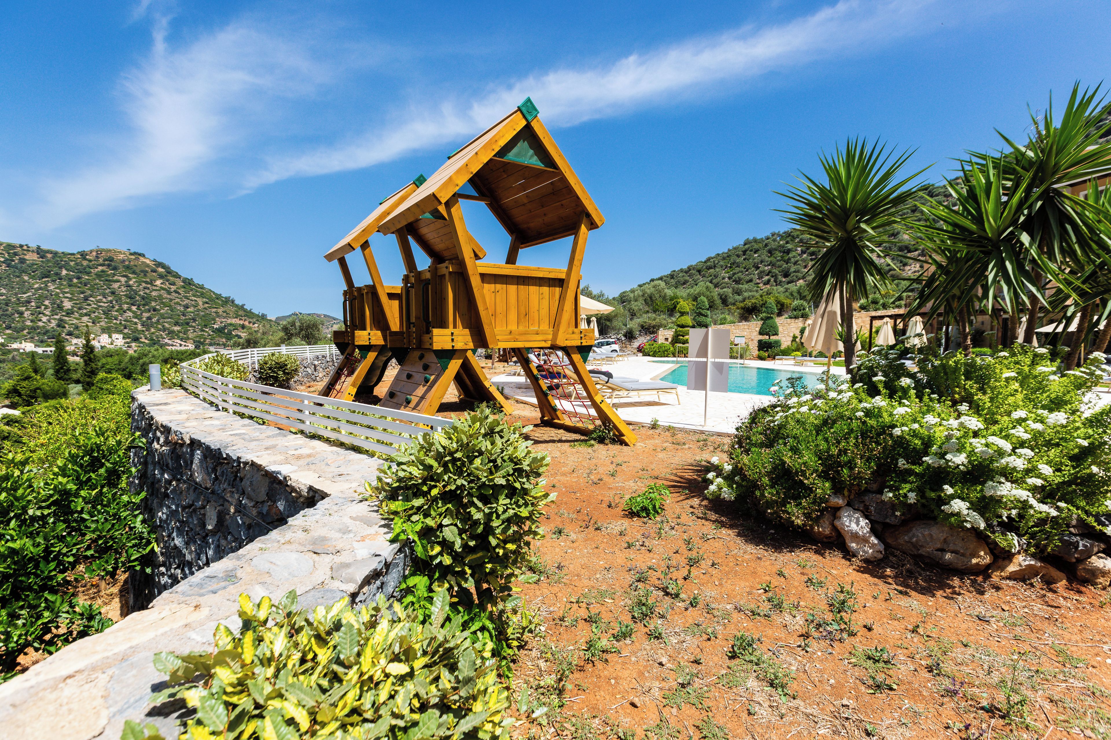 Estrutura de recreação de madeira em área ajardinada, com piscina e montanhas ao fundo.
