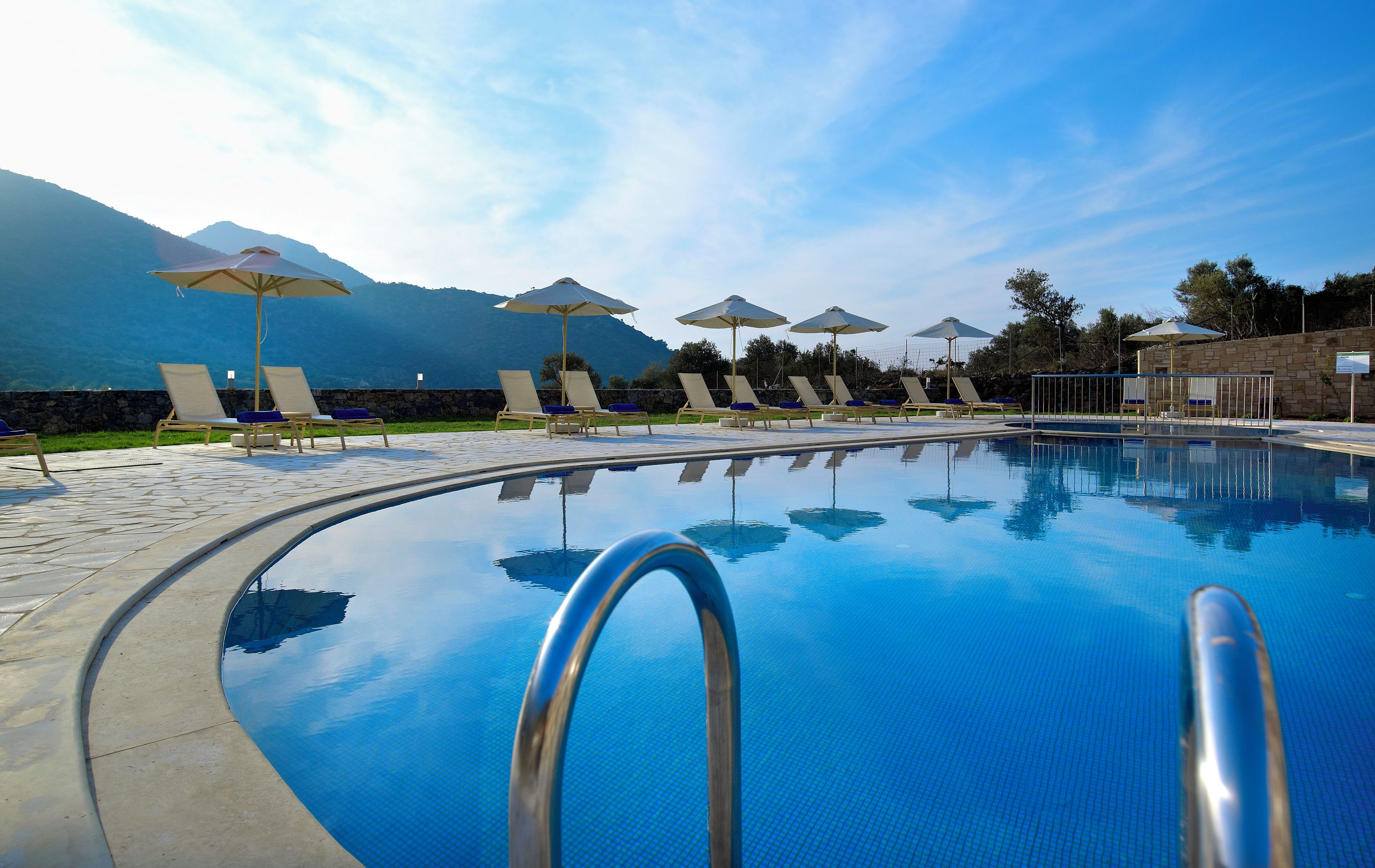 Piscina com espregui çadeiras e guarda-sóis, rodeada por montanhas.