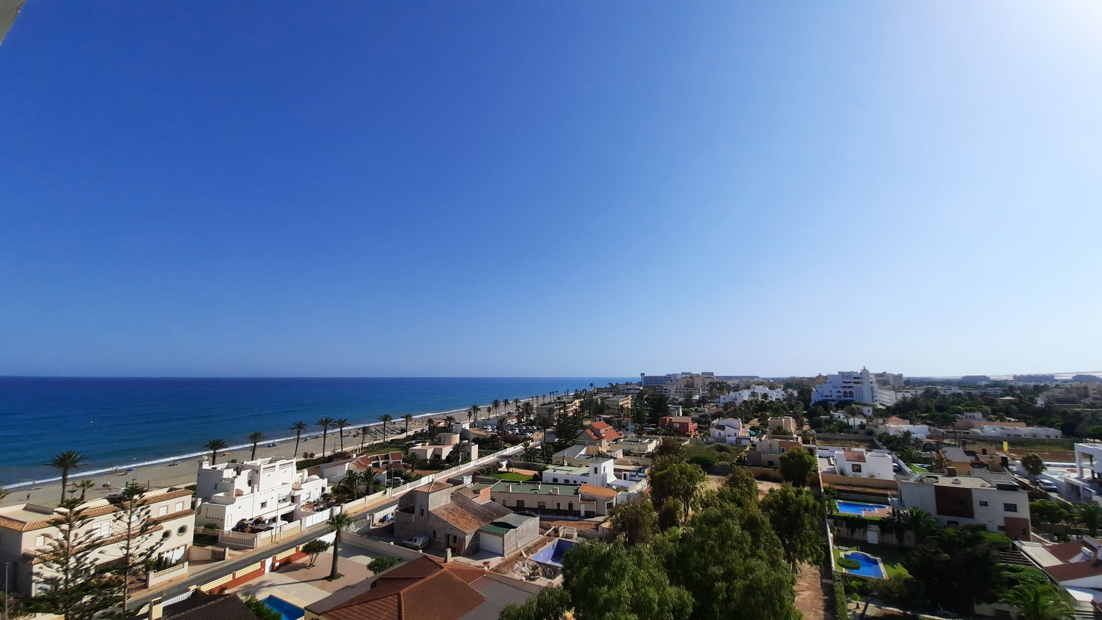 Uma vila costeira com uma praia, edifícios brancos e um céu azul límpido.