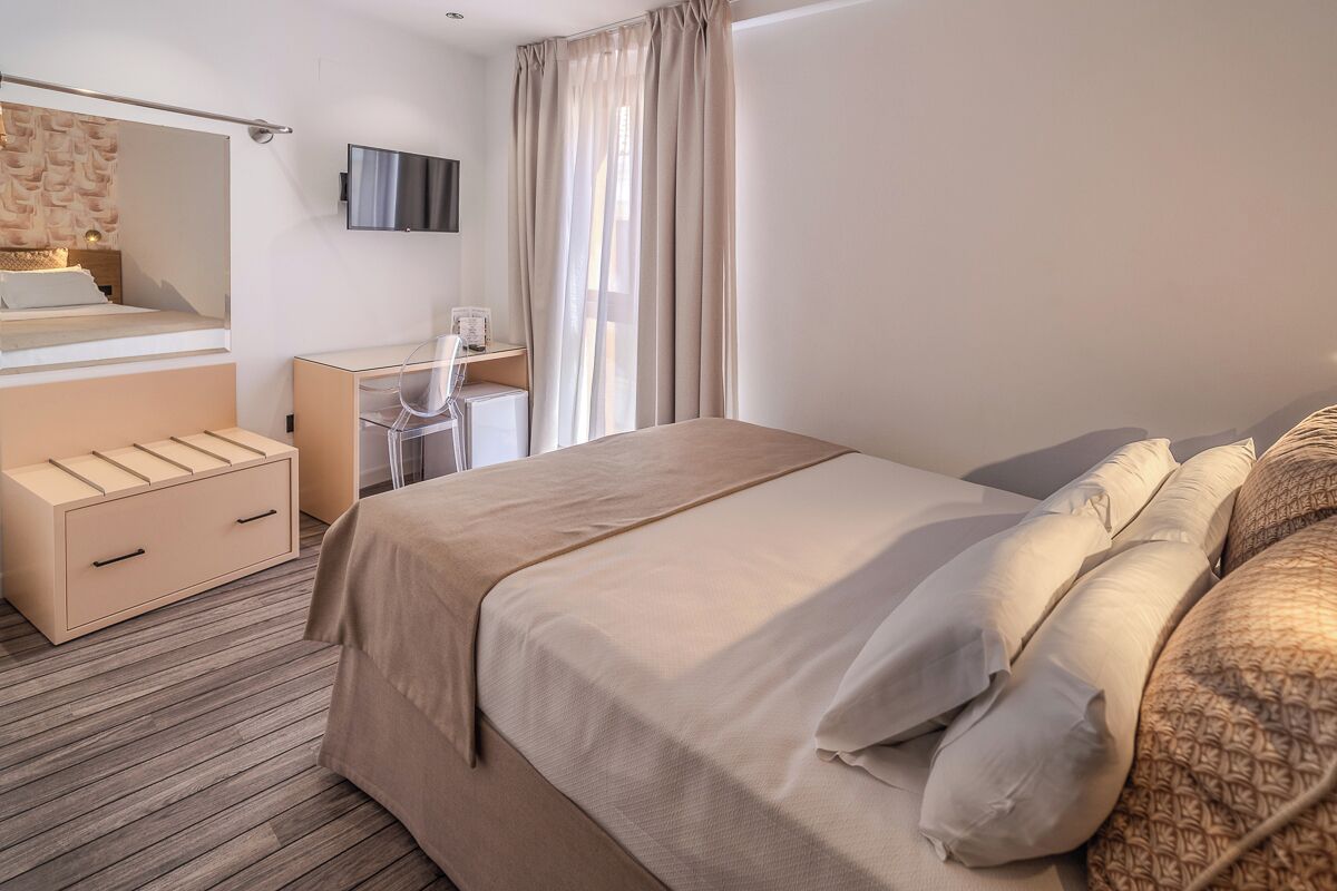 Quarto de hotel com cama, escrivaninha, cadeira, espelho e televisão.