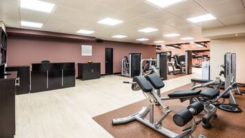 Uma academia com diversos equipamentos de exercício, uma mesa de recepção e um mural na parede.