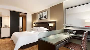 Quarto de hotel com cama, escrivaninha com cadeira, espelho grande e quadro na parede.