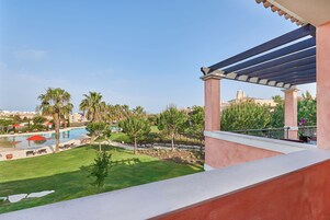 Uma varanda com vista para uma piscina, palmeiras e um edifício ao longe.