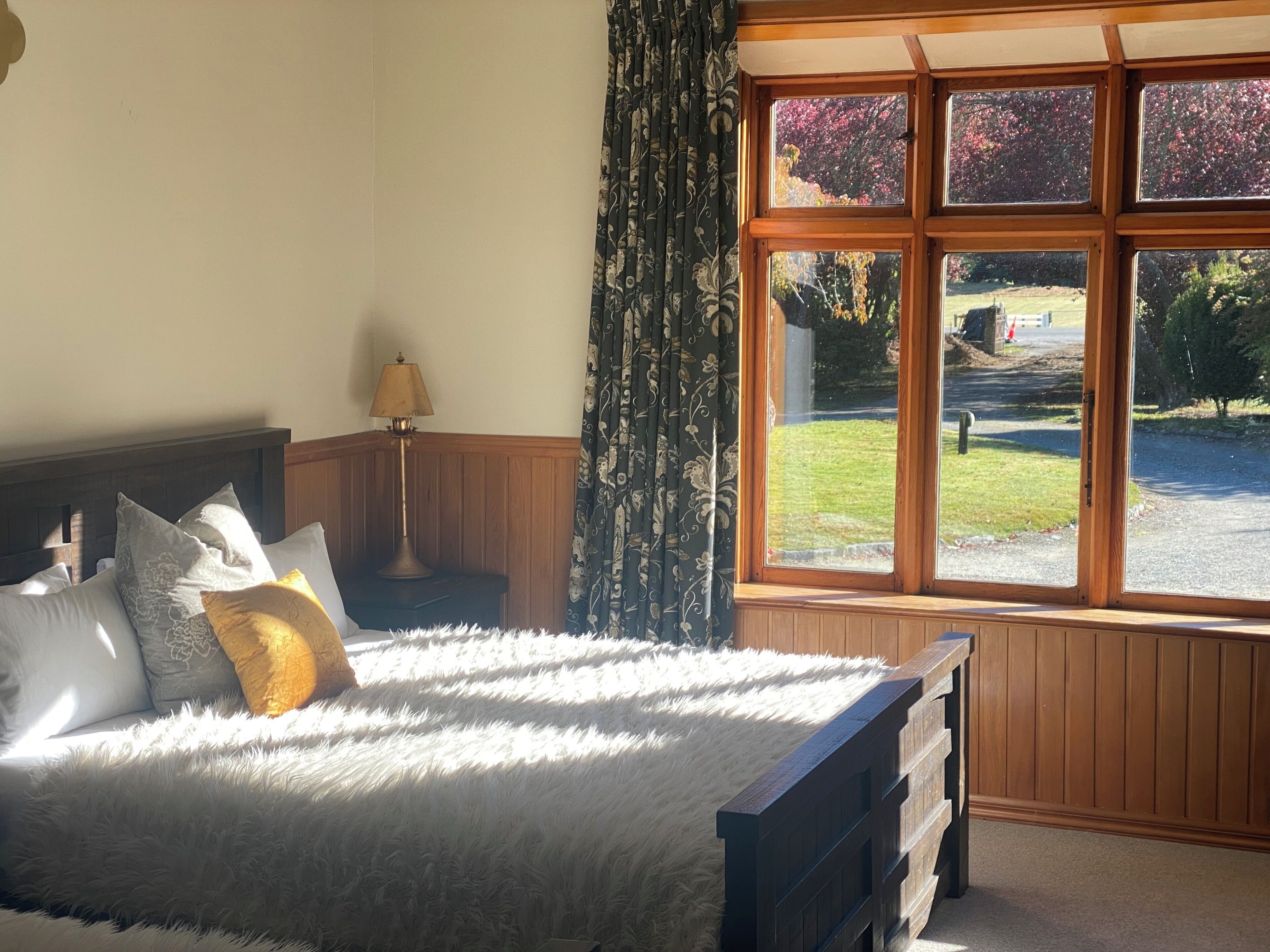 Quarto com cama grande, mesa de cabeceira, abajur e janela com vista para um jardim.