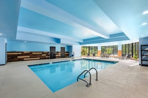 Piscina interna com águas azuis cristalinas, área de lazer com cadeiras e mesas, e amplas janelas com vista para o verde lá fora.