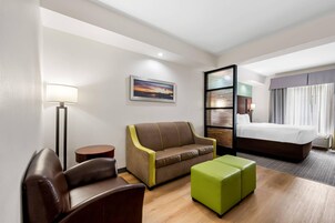 Quarto de hotel com cama, sofá, cadeira, mesa pequena e abajur.
