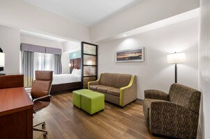 Quarto de hotel com cama, escrivaninha, cadeira, sofá e poltrona estampada.