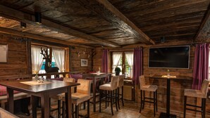 Interior rústico em madeira com área de bar, piso em ladrilho de pedra e uma grande televisão de tela plana presa à parede.