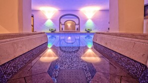 Uma área de piscina com chão em mosaico, duas luzes fixadas na parede e um arco central.