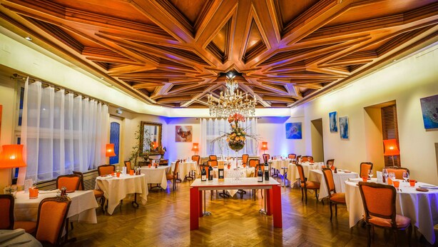 Uma sala de jantar com teto de madeira, mesas, cadeiras e lustres.