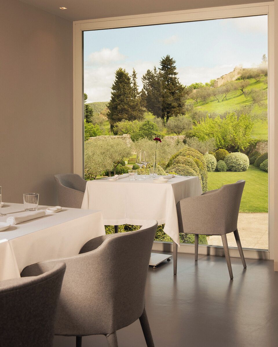 Uma área de jantar com uma mesa posta para dois, e uma janela com vista para um jardim paisagístico.
