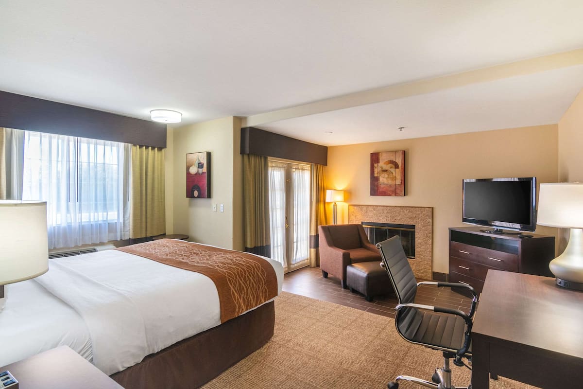 Quarto de hotel com uma cama grande, uma mesa, uma cadeira, uma televisão e uma lareira.