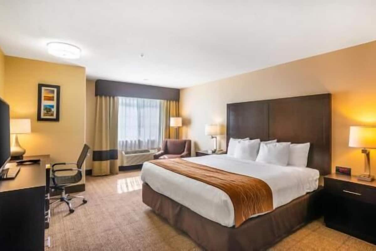 Quarto de hotel com uma cama grande, uma mesa, uma cadeira, uma televisão e uma janela com cortinas.