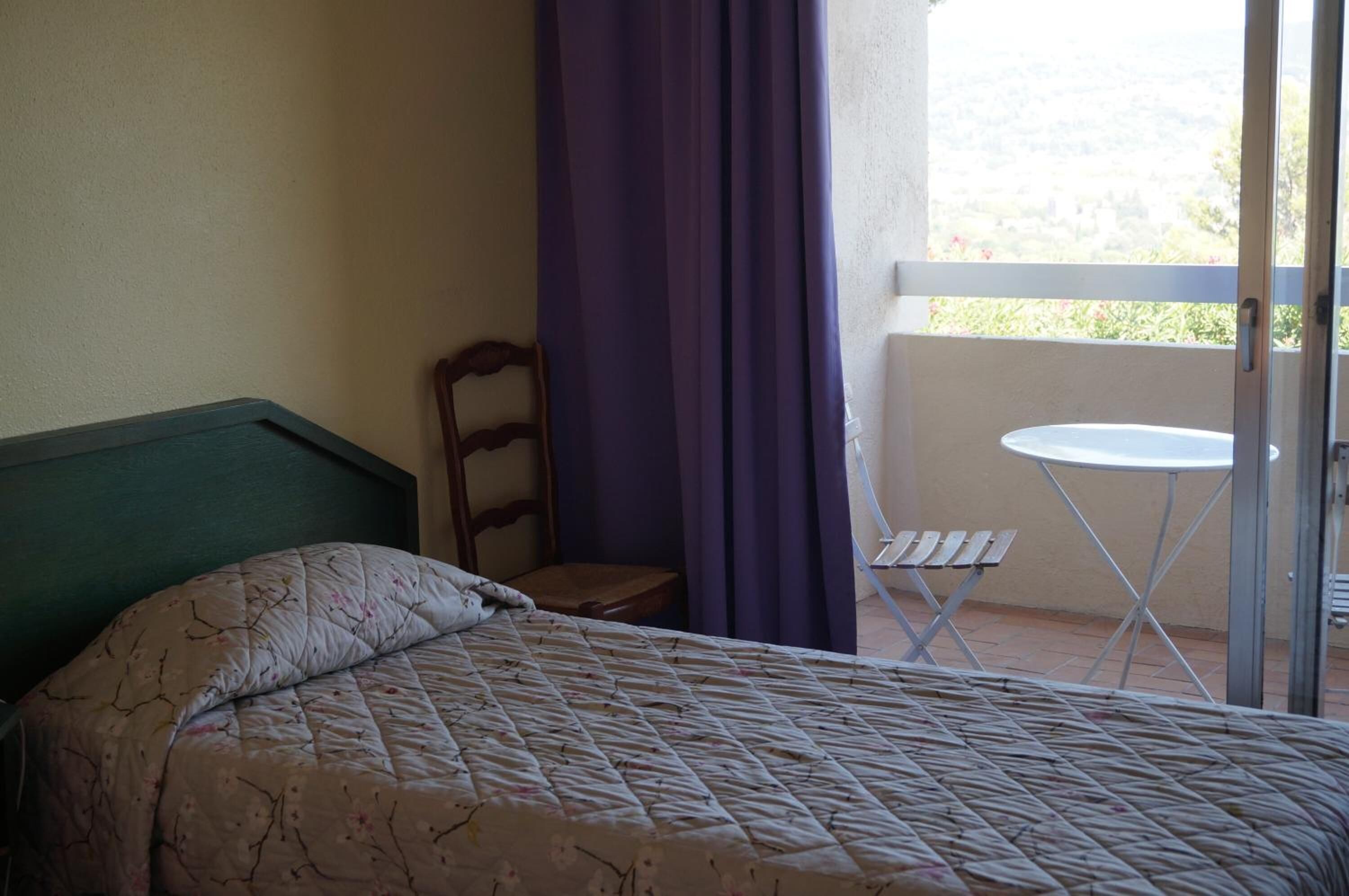 Quarto com cama, uma cadeira, mesa pequena e varanda com vista.