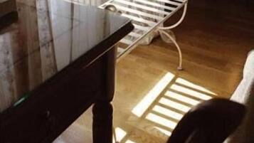 Quarto com uma mesa de madeira, uma cadeira de metal, um radiador e uma janela projetando padrões de luz no chão.
