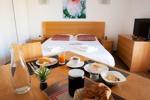 Mesa de café da manhã bem organizada, com uma garrafa de água, uma pequena planta, um croissant e diversos itens para o café.