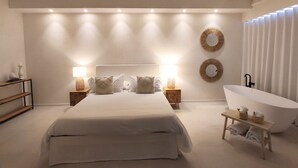 Um quarto moderno com uma cama grande, luminárias de cabeceira, um espelho fixado na parede e uma banheira de apoio.