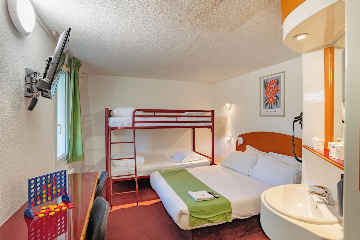 Quarto com beliche, escrivaninha, espelho e janela com cortinas.