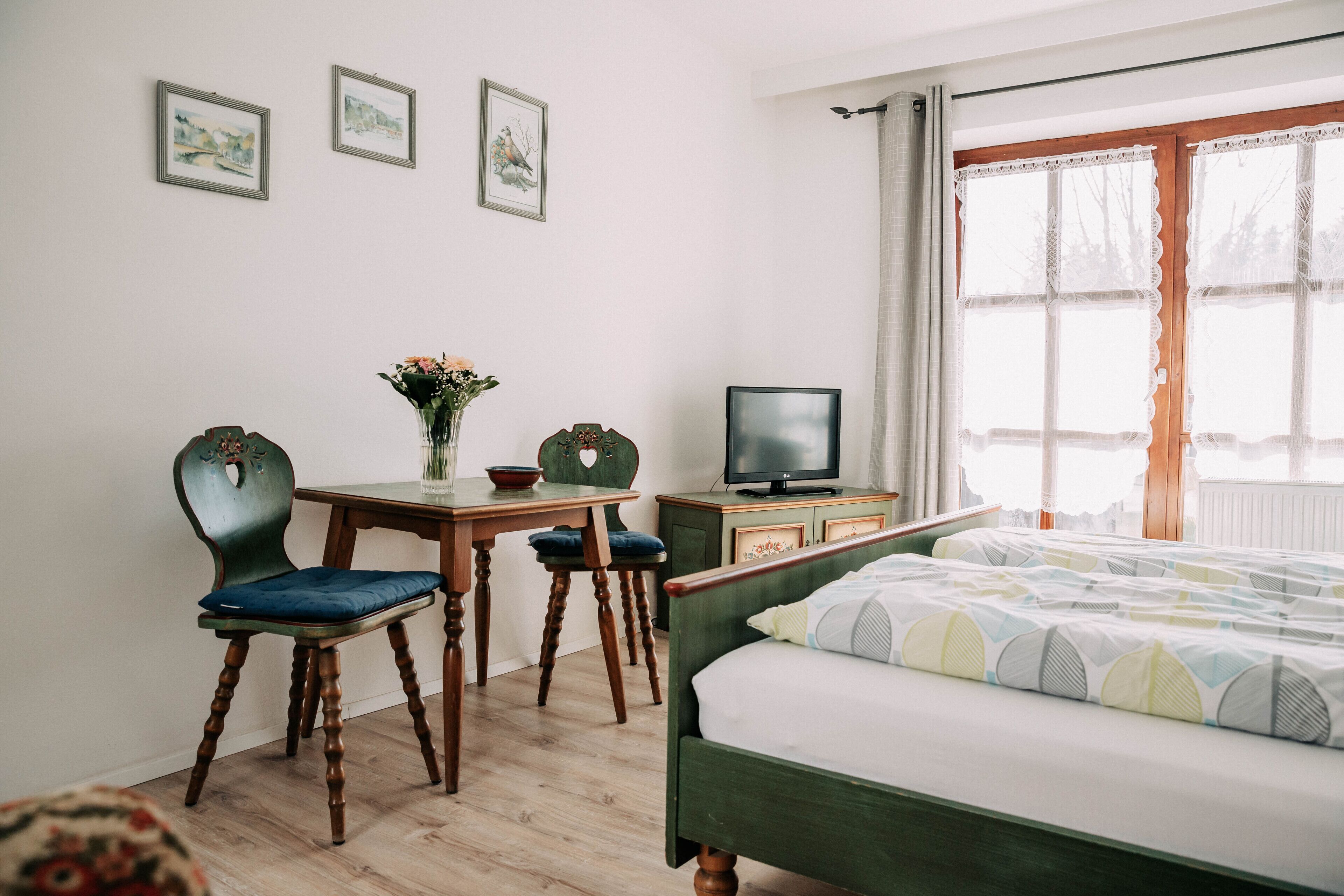 Quarto com cama, escrivaninha com cadeira, televisão e quadros na parede.