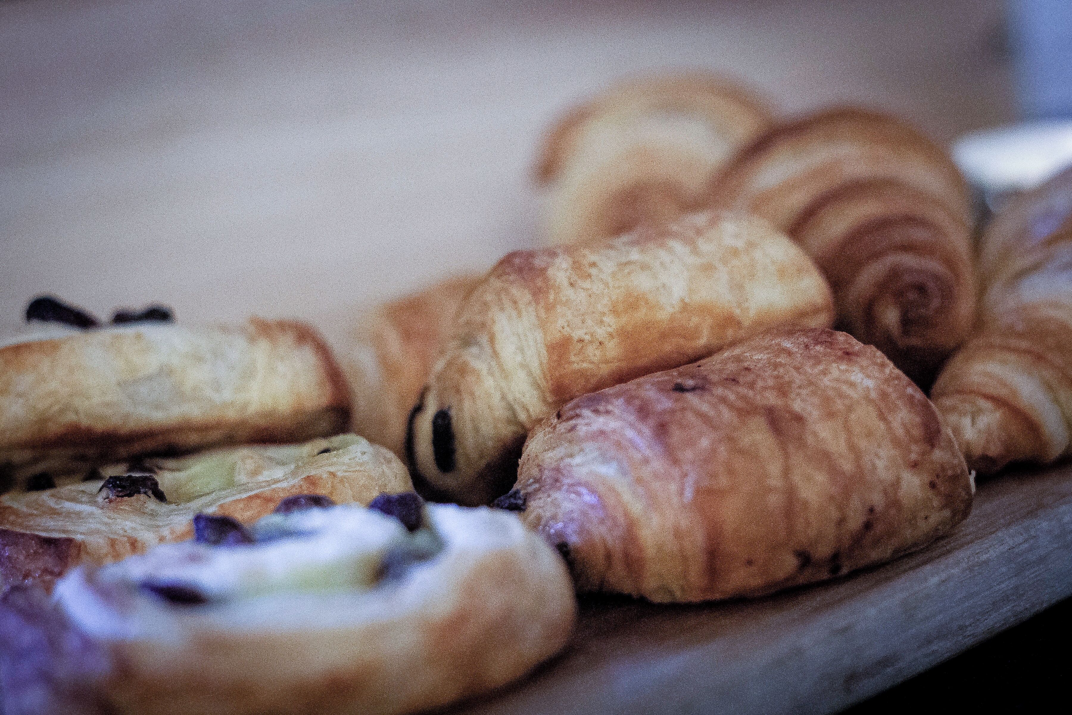 Uma bandeja de madeira com diversos doces, incluindo croissants e um pastel recheado.
