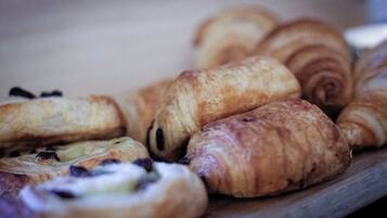 Uma bandeja de madeira com diversos doces, incluindo croissants e um pastel recheado.