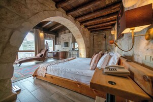 Quarto com uma cama grande, uma mesa de cabeceira de madeira, um telefone e um arco de pedra.