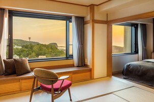 Quarto de hotel com uma grande janela, uma cama, uma cadeira e vista para a paisagem.