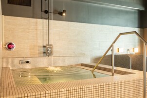 Uma área de spa moderna com hidromassagem, um display visível da temperatura da água e uma placa indicando o uso do botão WACCA.