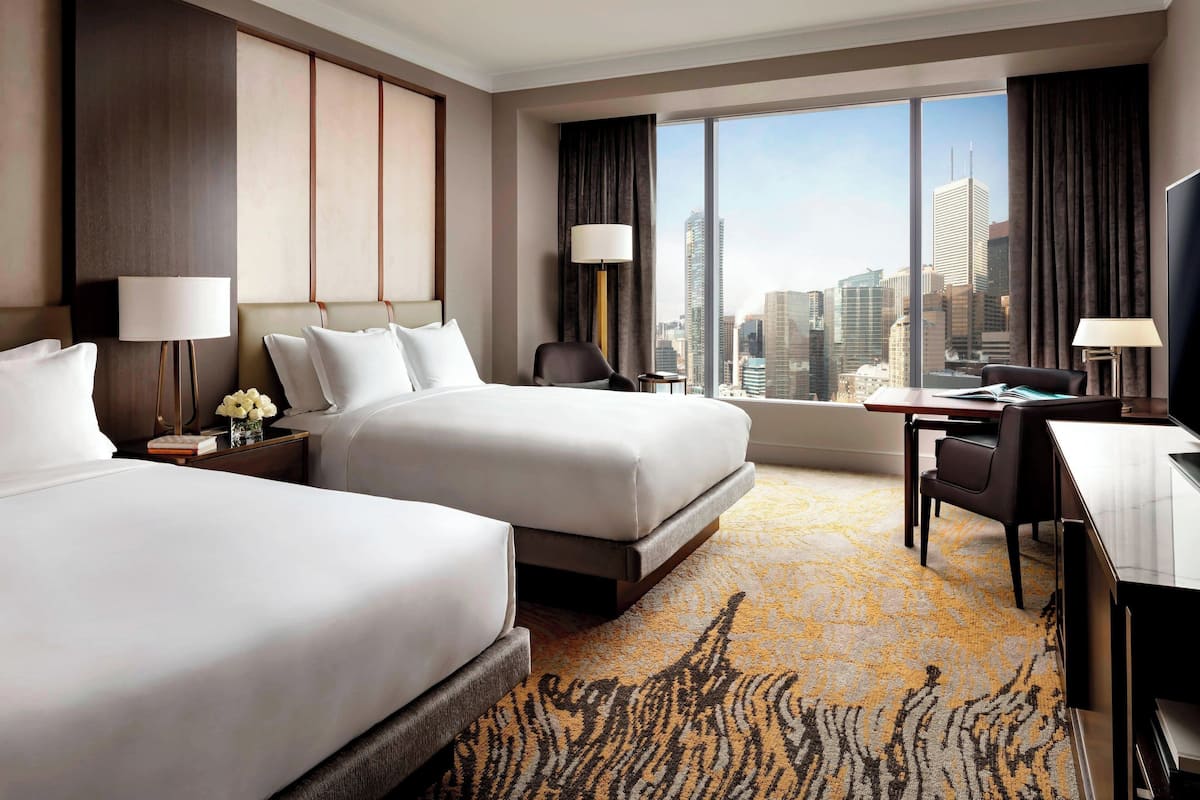 Quarto de hotel com duas camas, uma escrivaninha e uma janela grande com vista para a cidade.