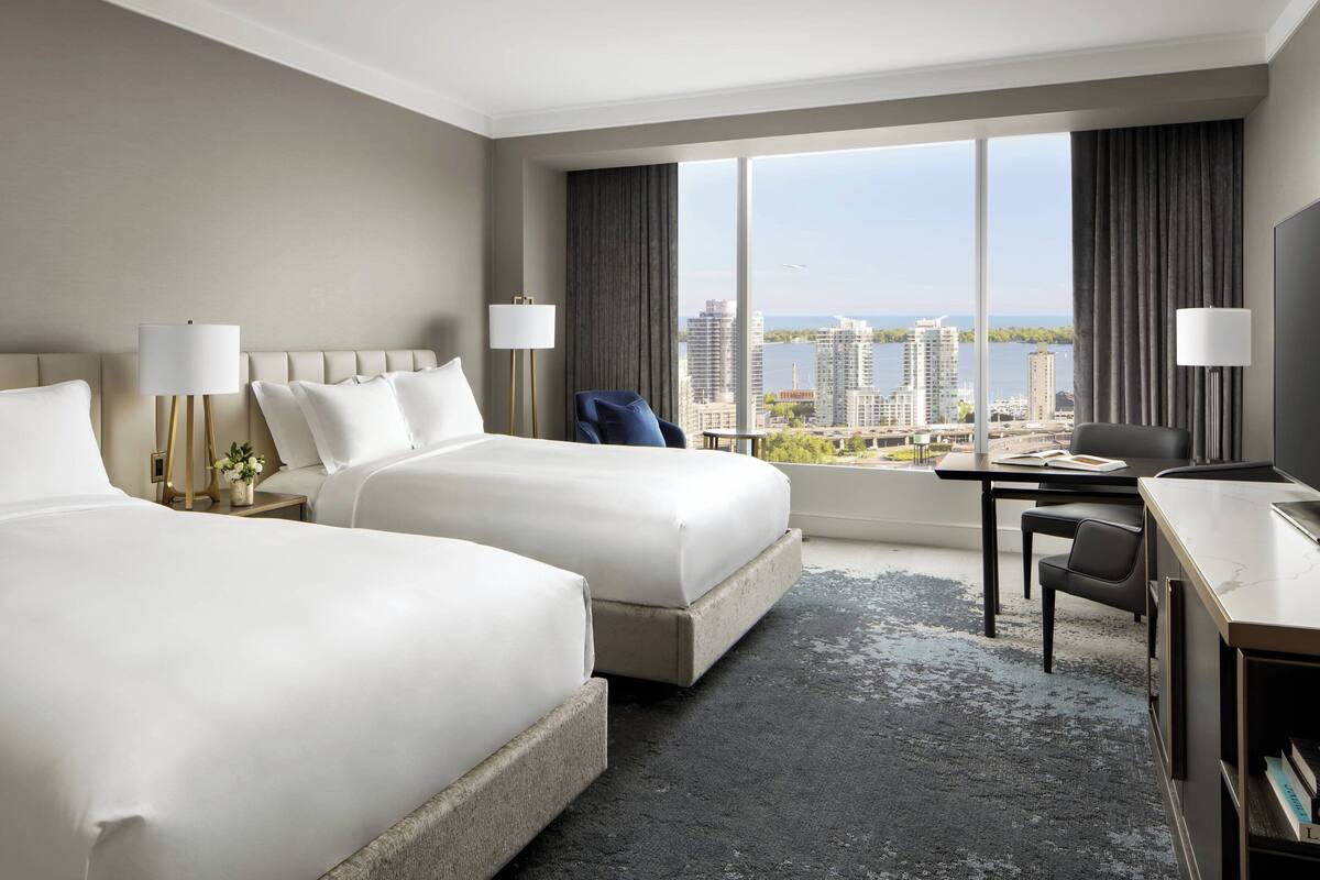 Quarto de hotel com duas camas, uma escrivaninha e vista para a cidade.