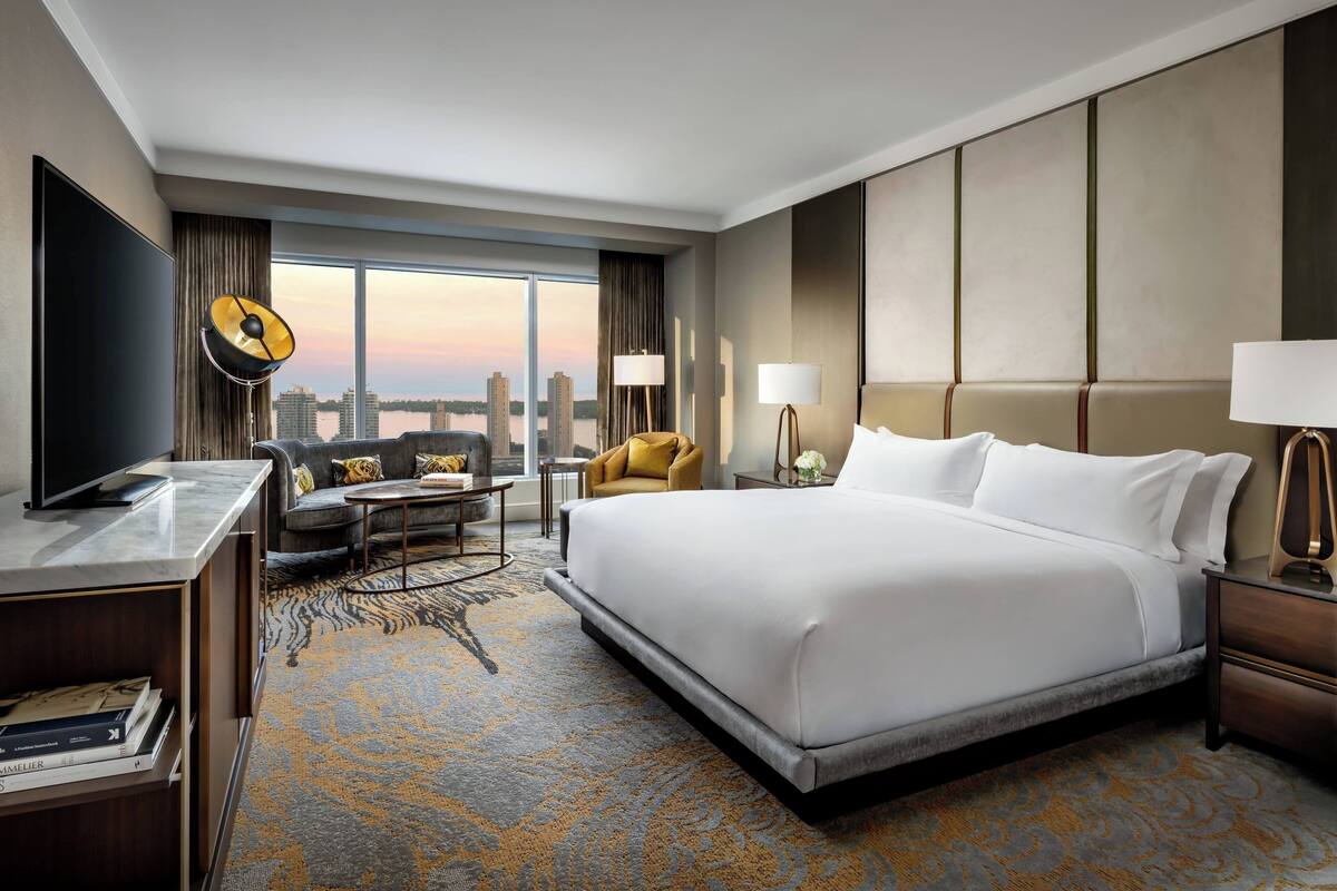 Quarto de hotel com uma cama grande, um sofá, uma TV e vista para a cidade.
