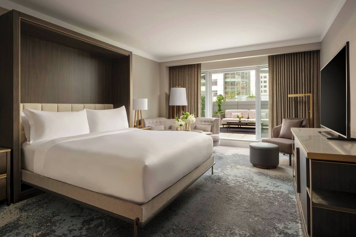 Quarto de hotel moderno com uma cama grande, uma escrivaninha, uma cadeira, uma televisão e vista para a cidade.