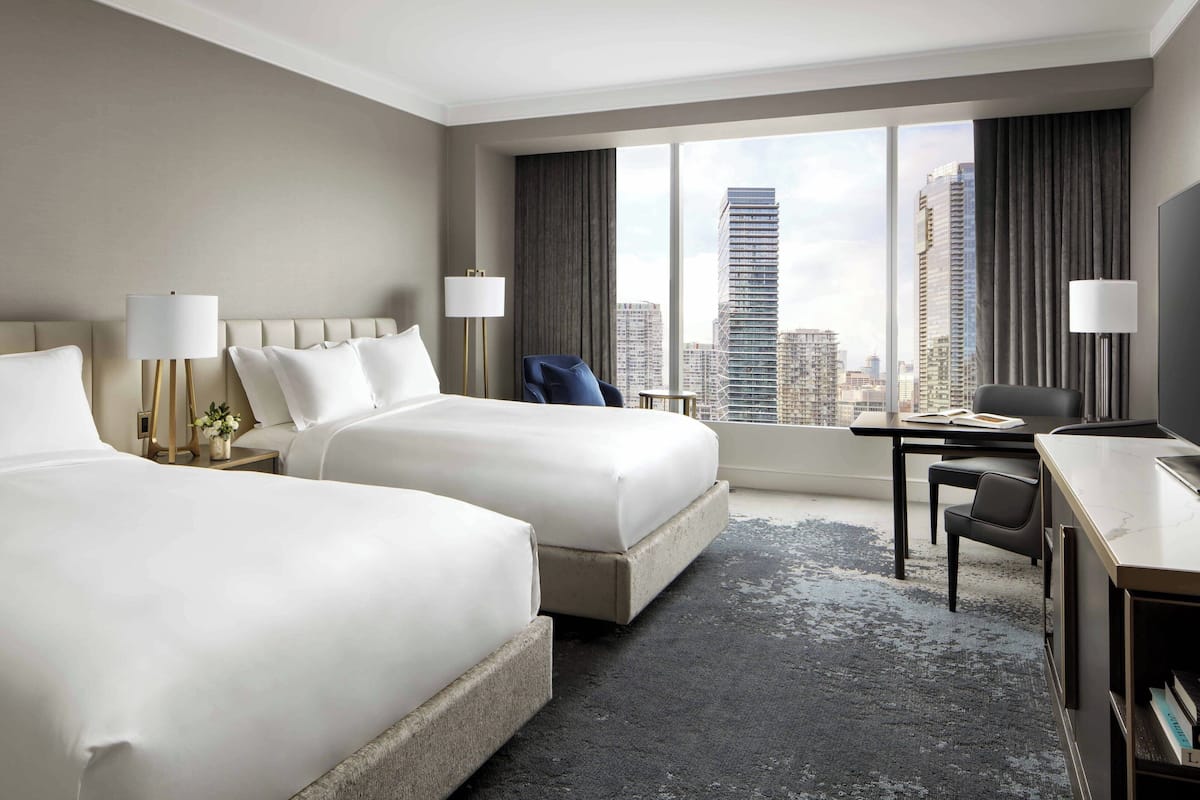 Quarto de hotel com duas camas, uma escrivaninha e vista para o horizonte da cidade.