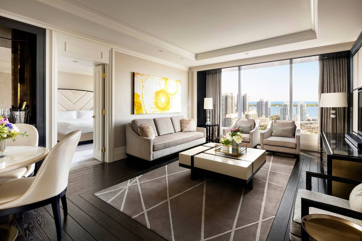 Quarto de hotel moderno com vista para a cidade, um sofá, uma mesa de centro e um espaço de refeições com cadeiras e uma mesa.