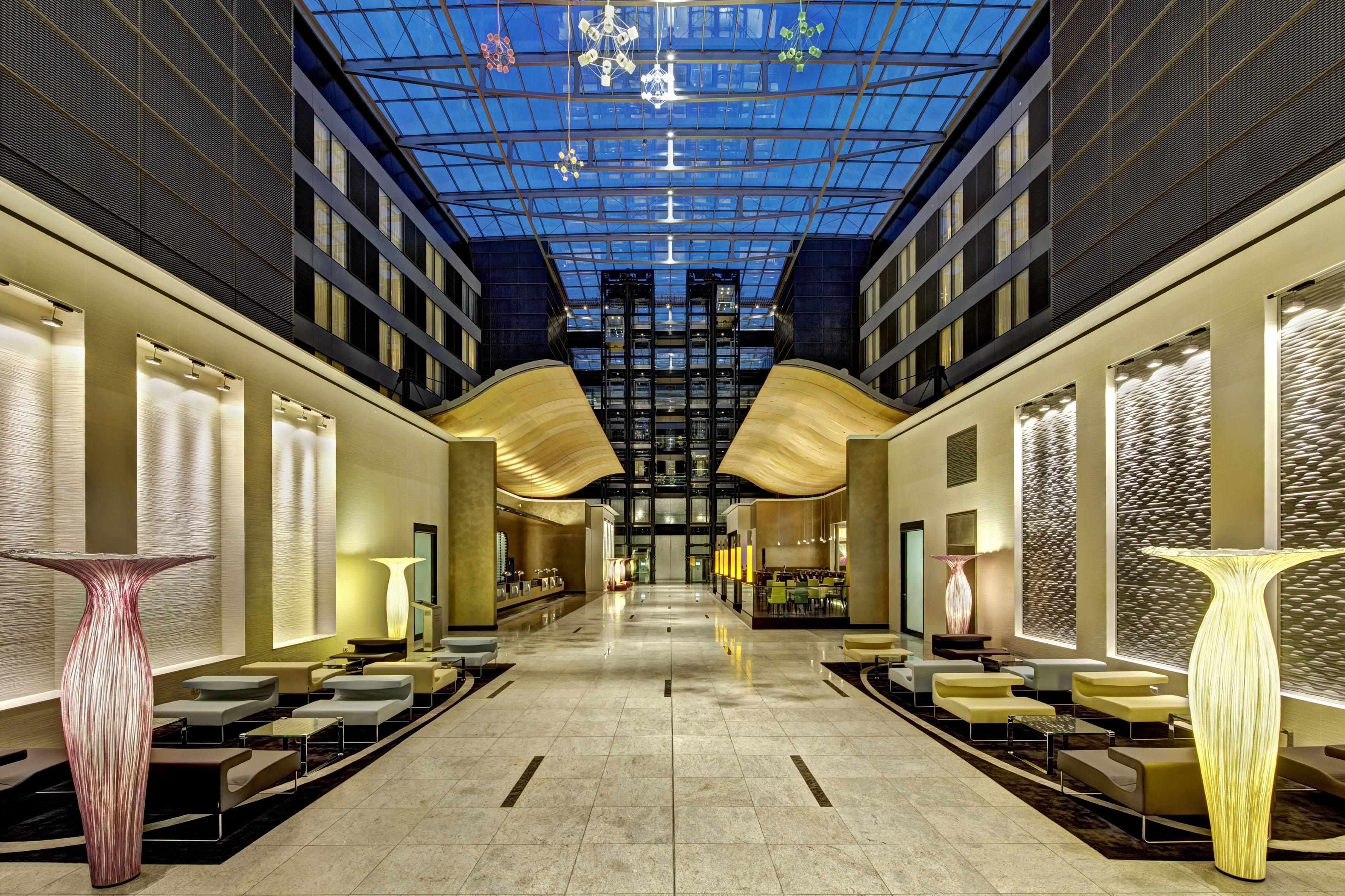 Um hall de hotel moderno com teto alto, painéis de vidro e mobiliário contemporâneo.