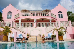 Um edifício rosa com piscina, varandas e espreguiçadeiras.