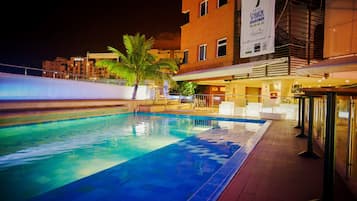 Piscina com uma palmeira, um edifício com uma placa e área de estar ao ar livre.