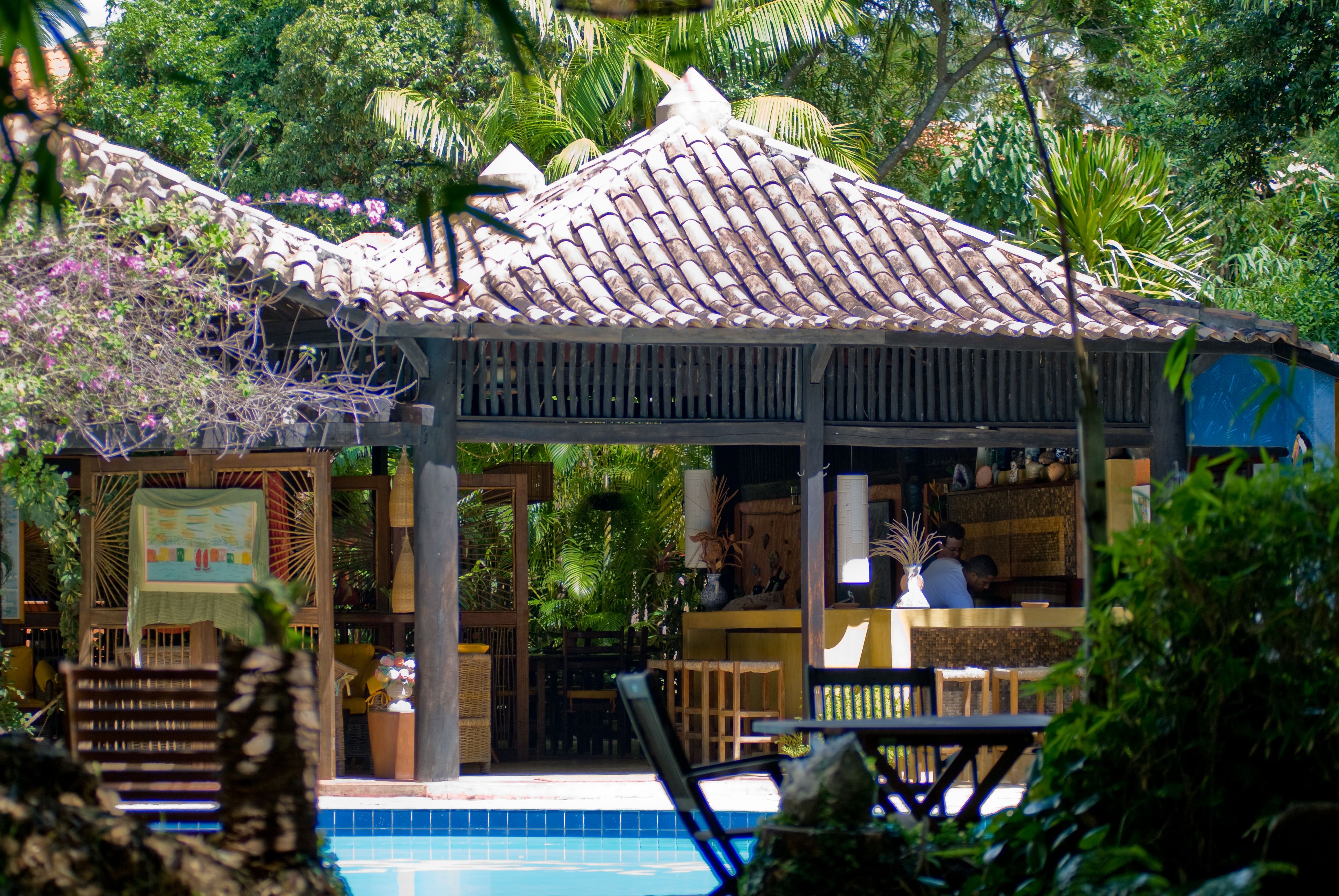 Uma área externa coberta com piscina, assentos de madeira e vegetação exuberante.
