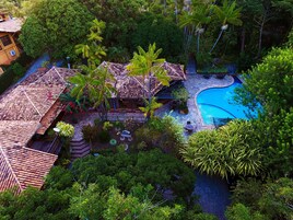 Um resort tropical com piscina, construções de palha e vegetação exuberante.