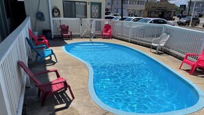 Piscina com cerca branca e cadeiras vermelhas ao redor.