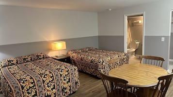 Quarto com duas camas, uma mesa e cadeiras. Há uma luminária em uma mesa de cabeceira.