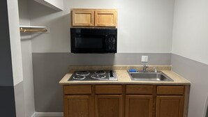 Uma cozinha compacta com armários de madeira, um micro-ondas preto, fogão a gás e uma pia.