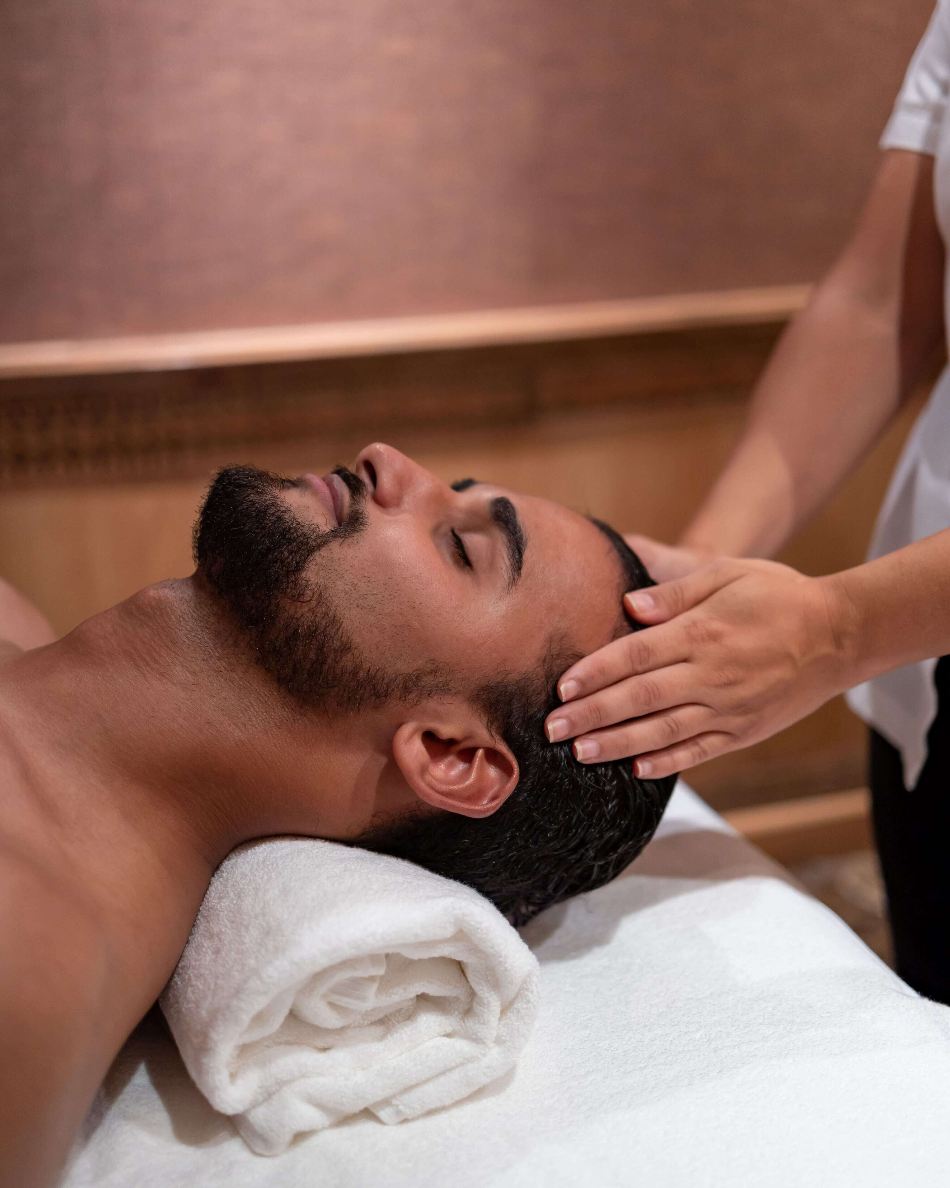 Uma pessoa deitada em uma cama, recebendo massagem e com uma toalha branca.
