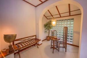 Quarto com um banco de madeira, uma mesa com cadeira, uma planta em vaso e uma janela com vista para o verde.